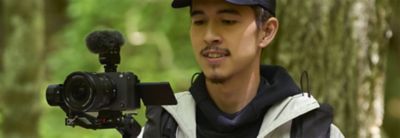 Mikrofon ve rüzgar siperi takılı, gimbal’a takılmış fotoğraf makinesiyle video çeken bir kullanıcının kullanım görüntüsü