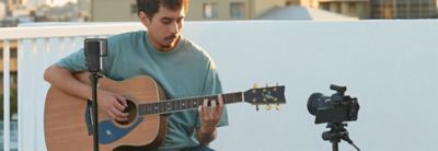 Açık havada gitar çalarken bir stant üzerindeki mikrofonla şarkı söyleyen adamı gösteren kullanım görüntüsü